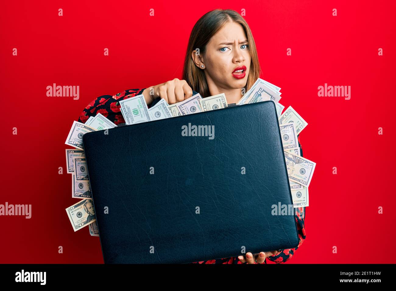 Beautiful young blonde woman holding briefcase full of dollars in shock ...