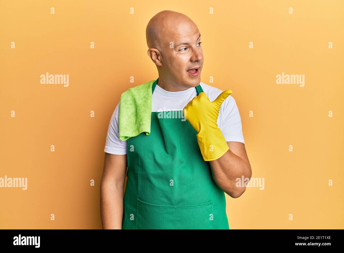 Middle age bald man wearing apron holding cleaning gloves smiling with ...