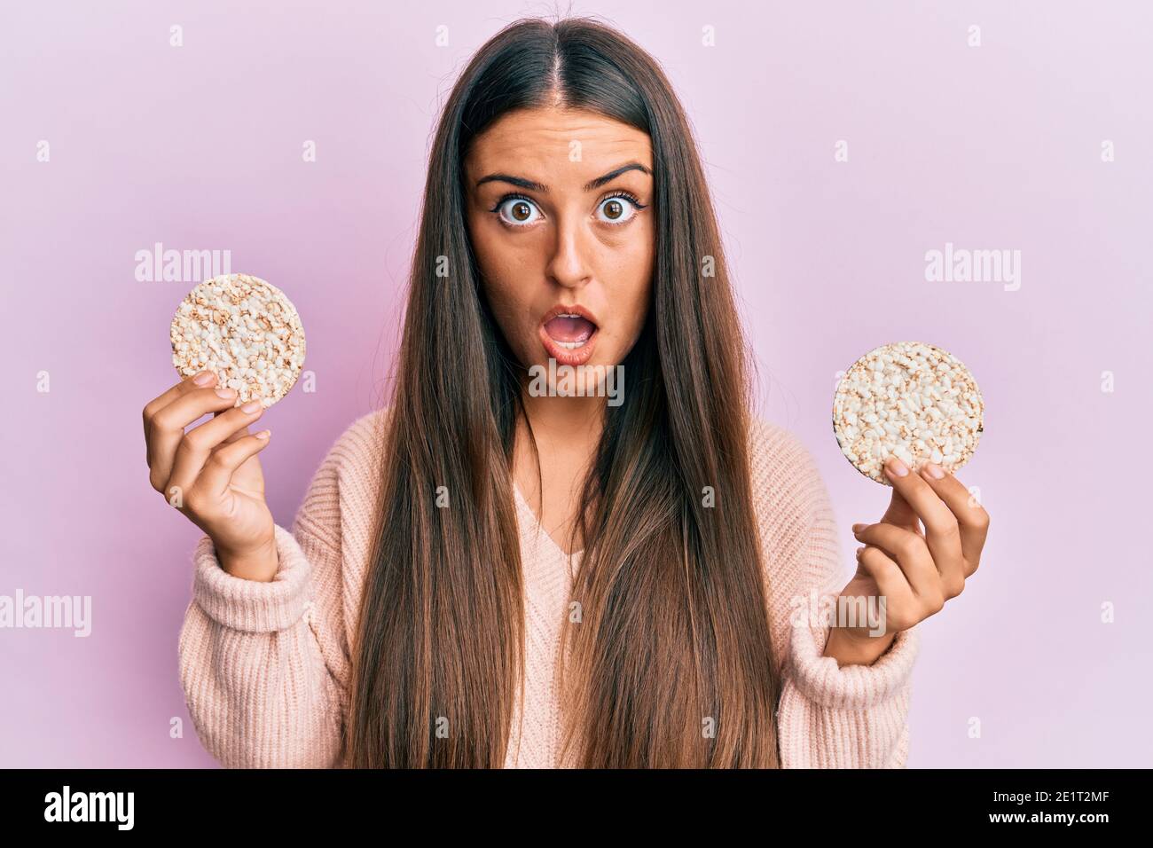 Beautiful hispanic woman eating healthy rice crackers afraid and ...