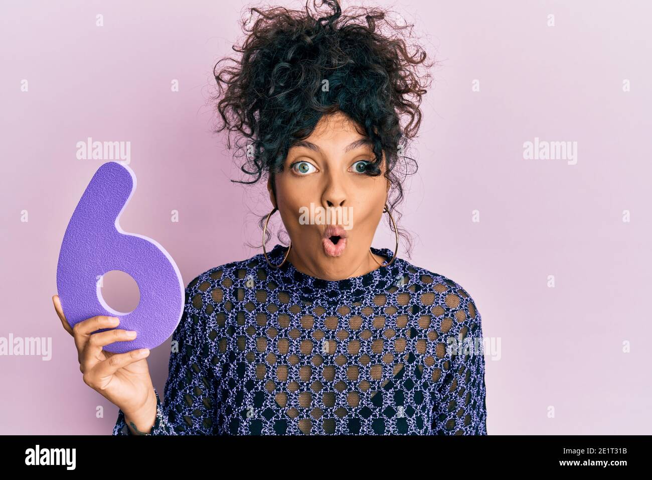 Young hispanic woman holding number six scared and amazed with open mouth for surprise ...