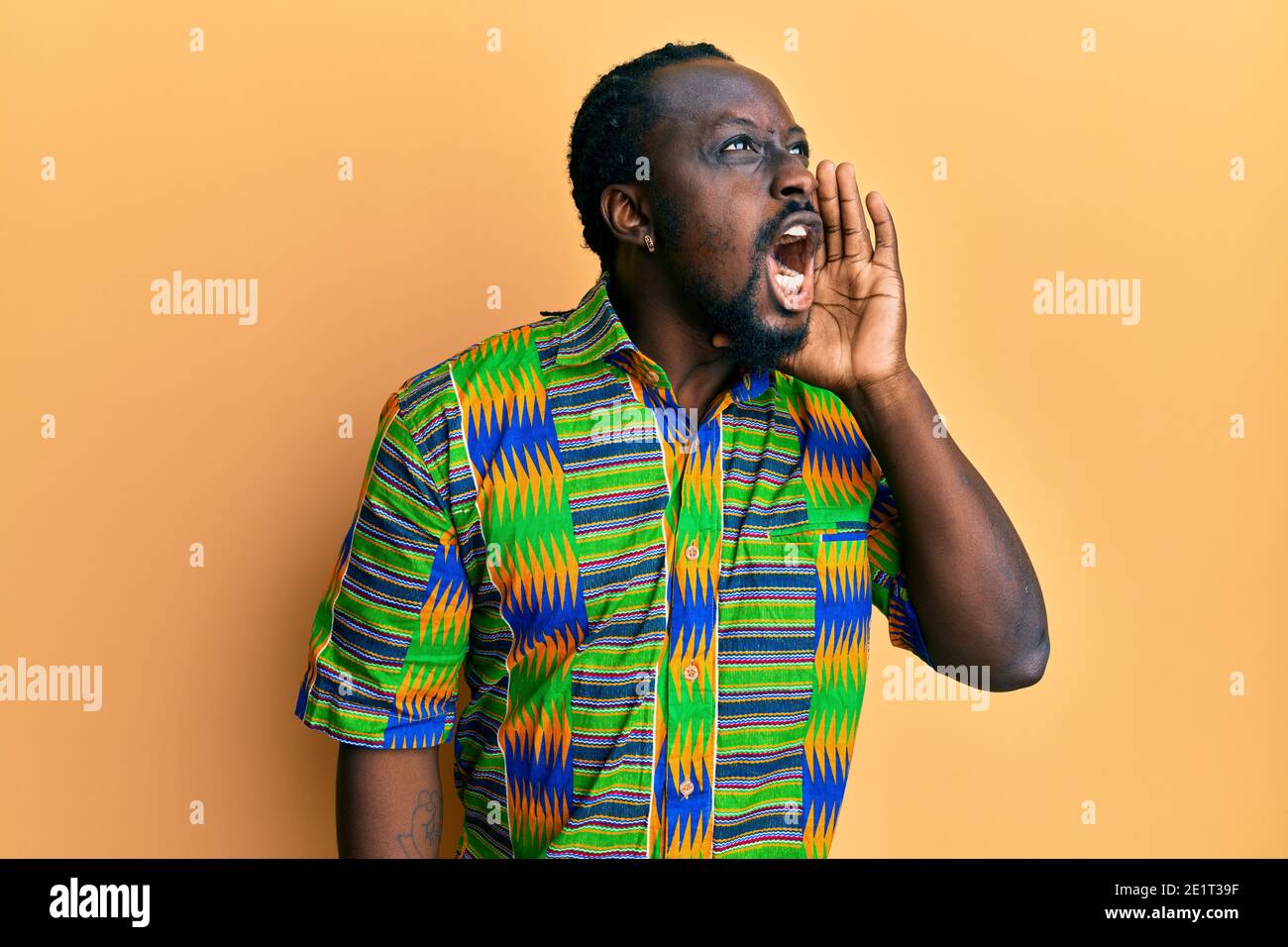 Handsome young black man wearing colorful ethnic clothes shouting and ...