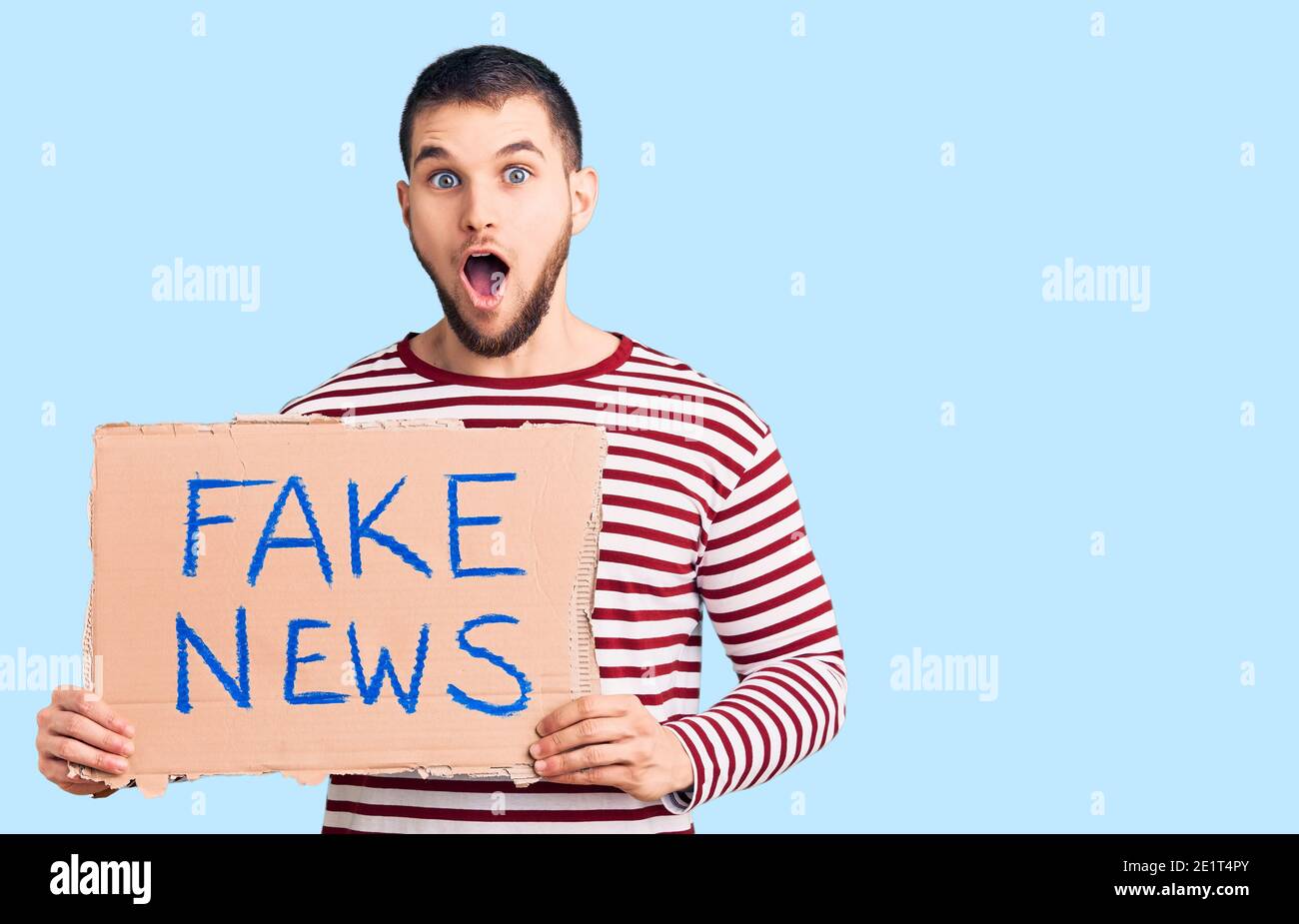 Young handsome man holding fake news message banner scared and amazed ...