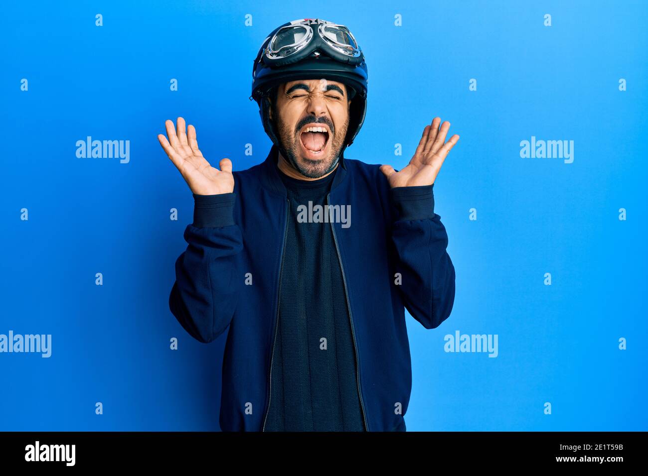Young hispanic man holding motorcycle helmet celebrating mad and crazy ...