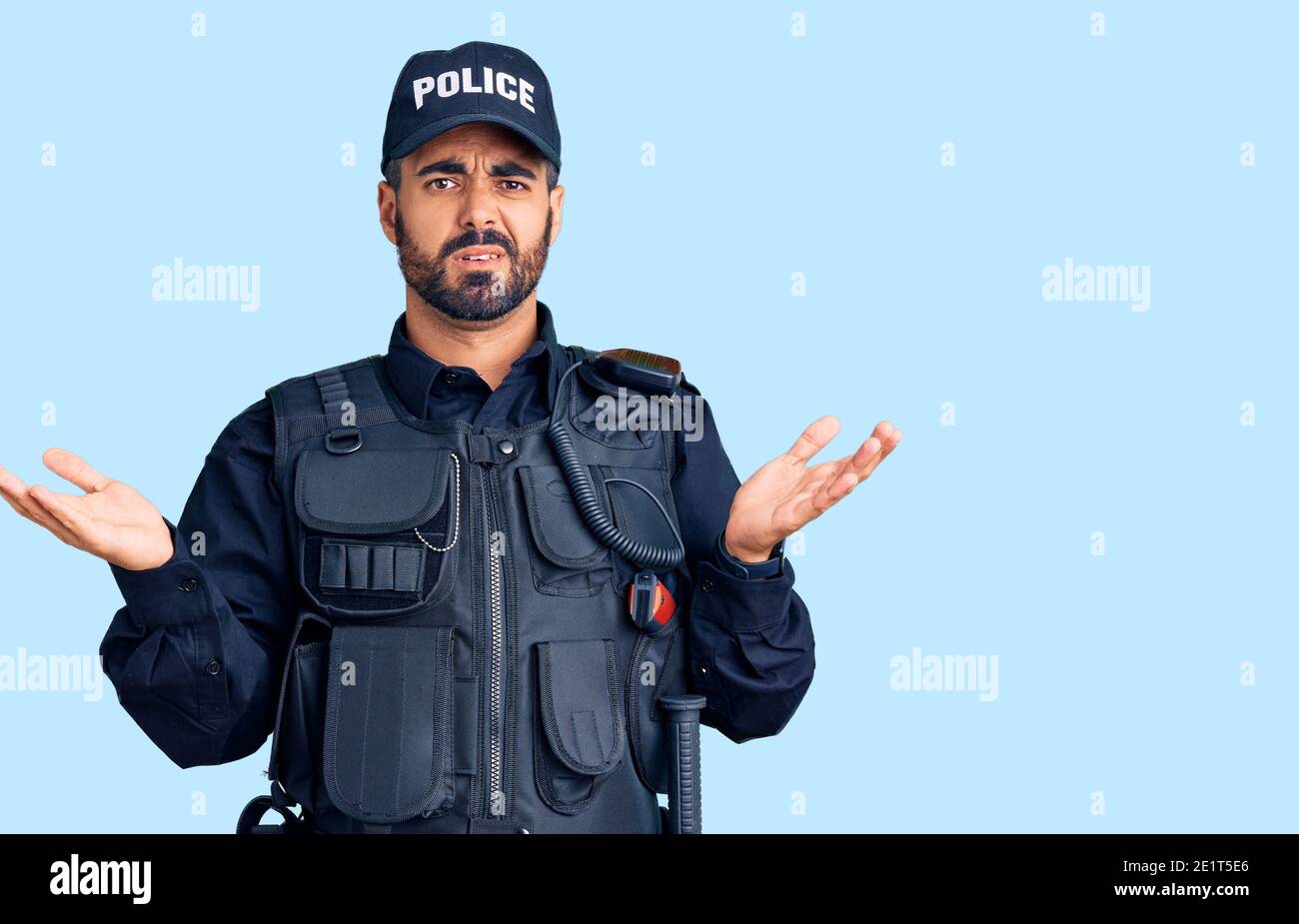 Young hispanic man wearing police uniform clueless and confused with ...