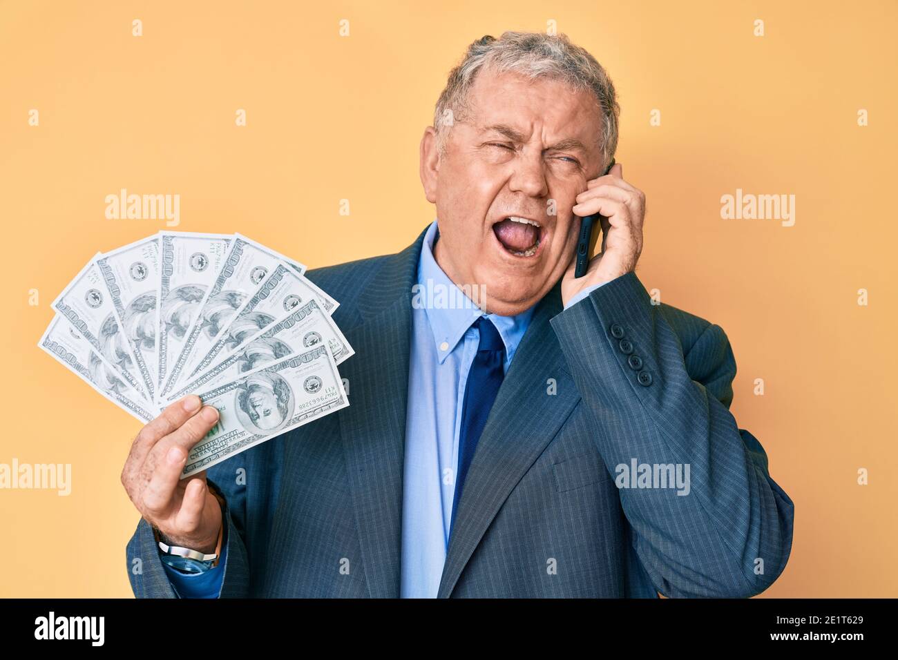 Senior grey-haired man wearing suit holding dollars and using ...