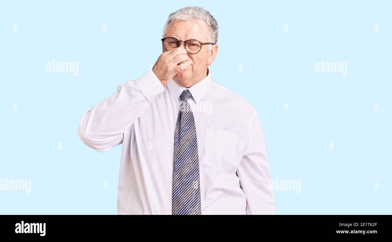 Senior grey-haired man wearing business clothes smelling something ...