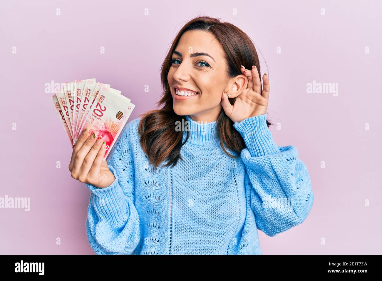 Young brunette woman holding 20 israel shekels banknotes smiling with ...