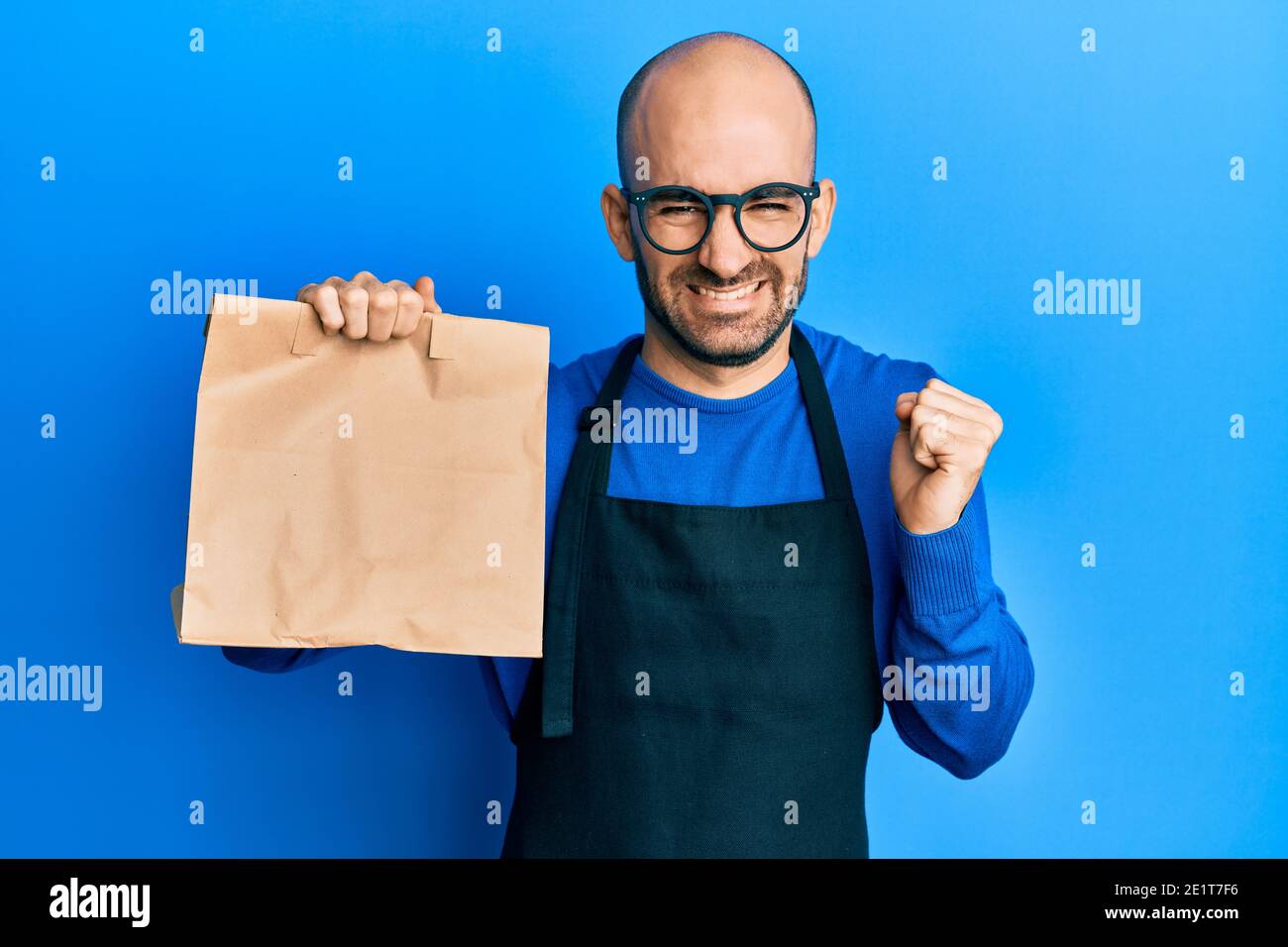 Young Hispanic Man Wearing Waiter Uniform Holding Take Away Paper Bag