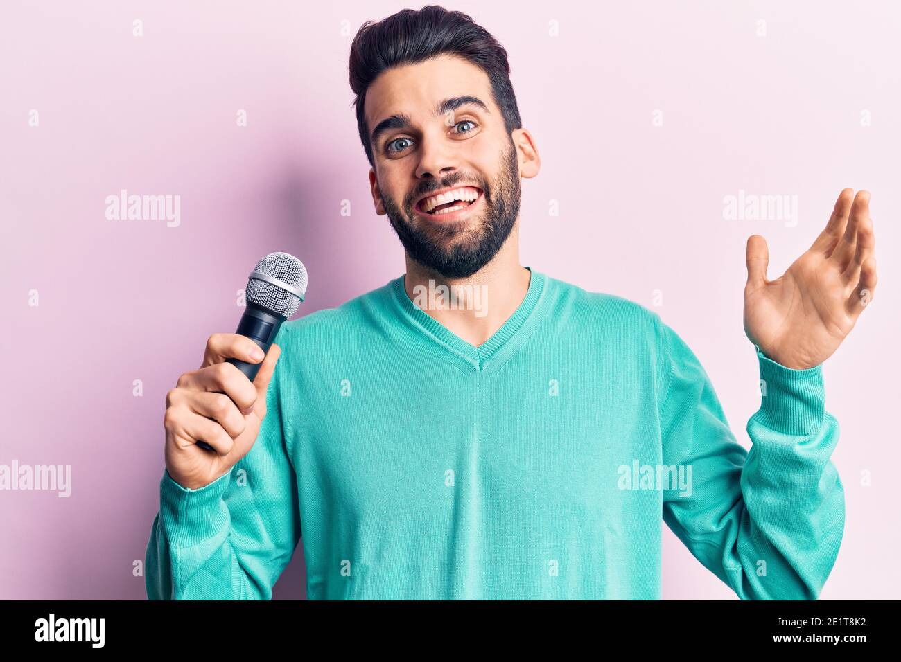 Young handsome man with beard singing song using microphone celebrating ...