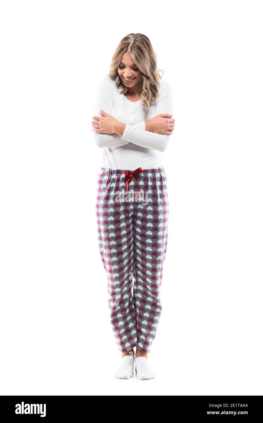Cute young cuddly woman in comfy pajama hugging herself smiling feeling ...