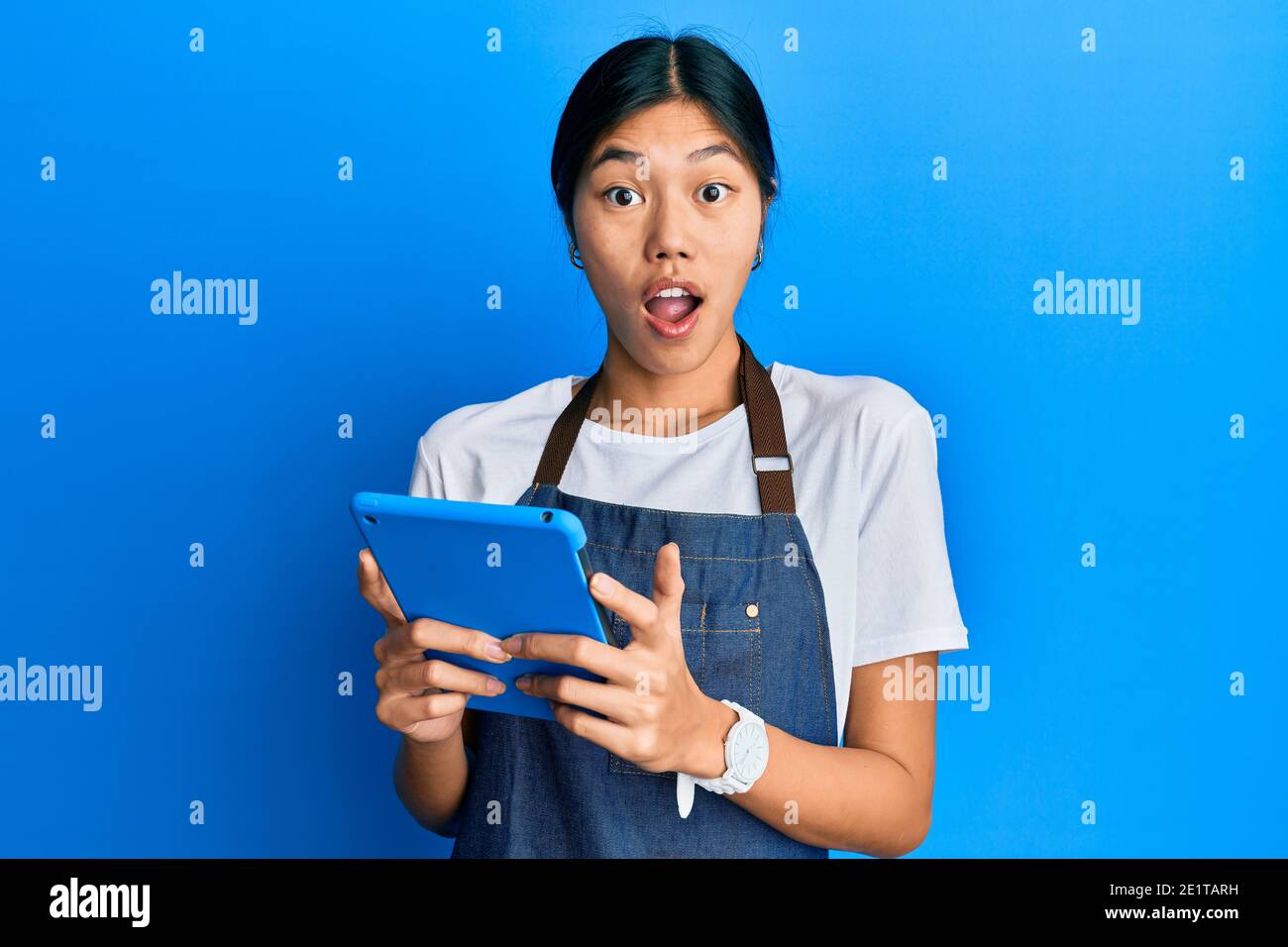 Young chinese woman wearing cook apron using touchpad afraid and ...