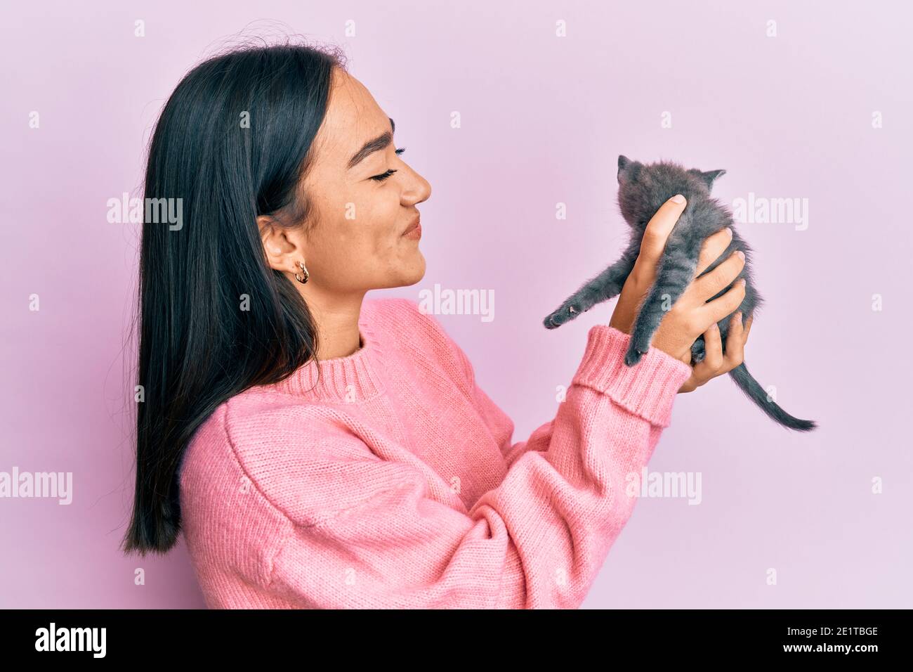 Young hispanic girl smiling happy holding cute cat over isolated pink ...