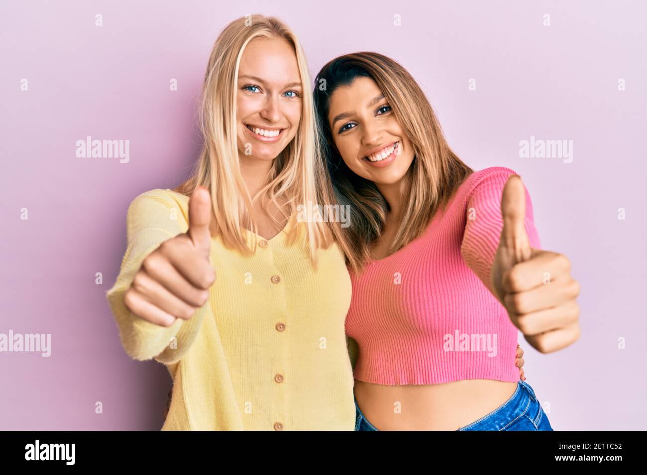 Two friends standing together over pink background approving doing ...