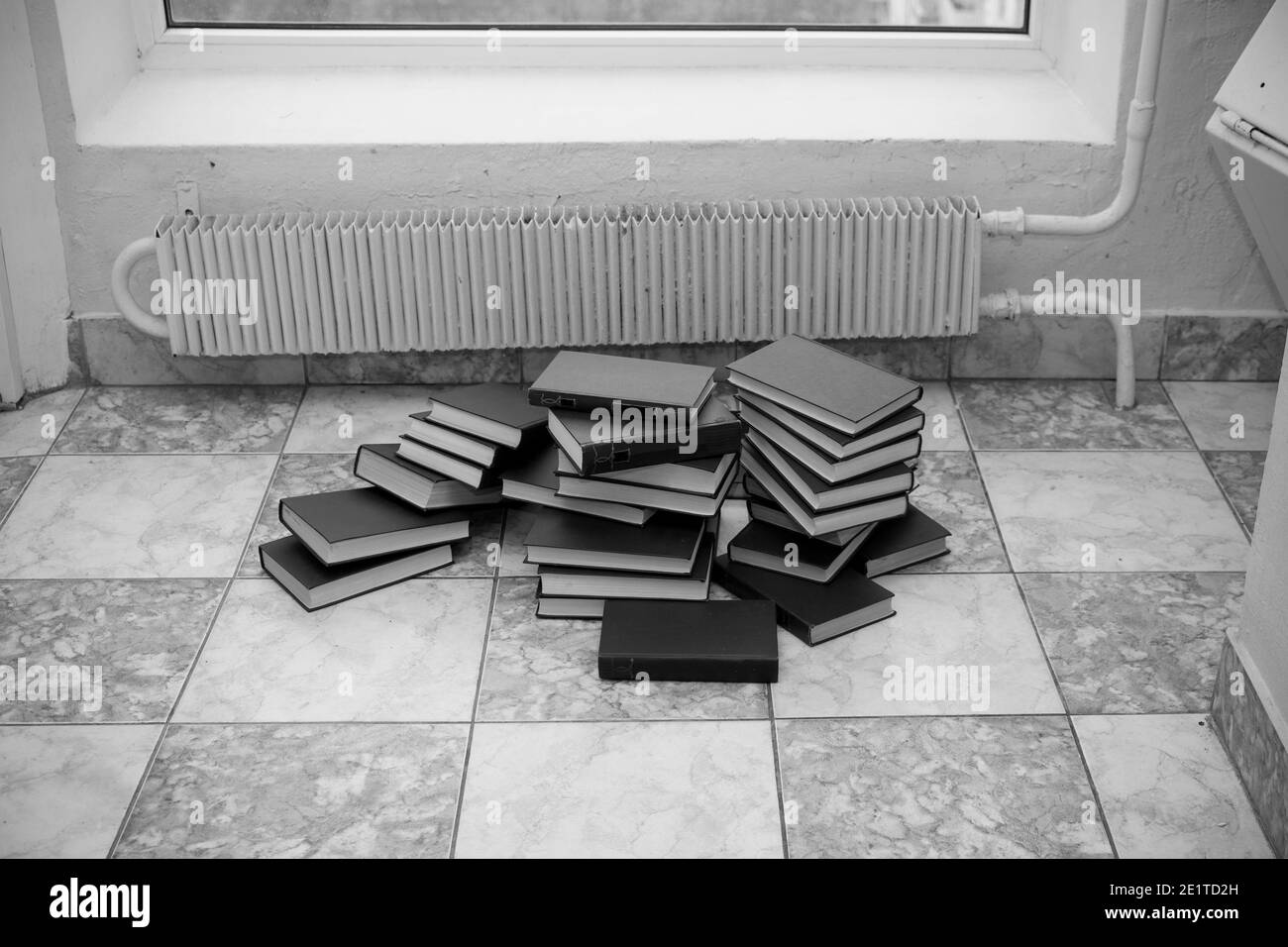 Pile of discarded old books on the tiled floor, in black and white ...