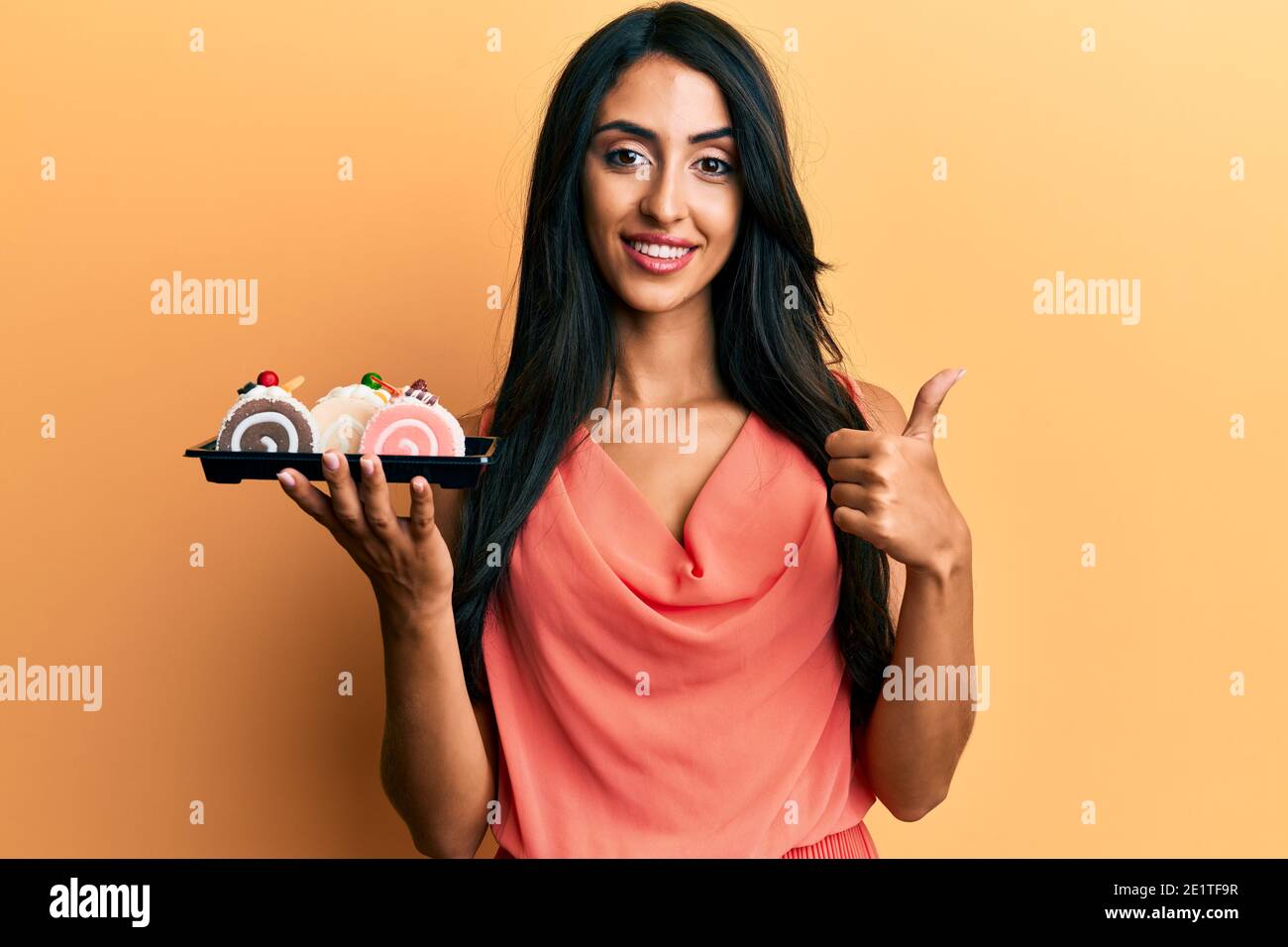 Beautiful hispanic woman holding cake sweets smiling happy and positive ...