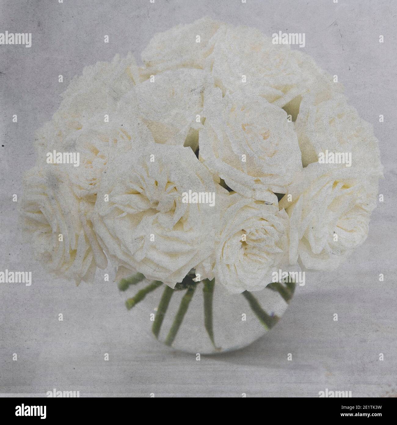 Bouquet of white roses in a round glass vase on a beige table against a ...