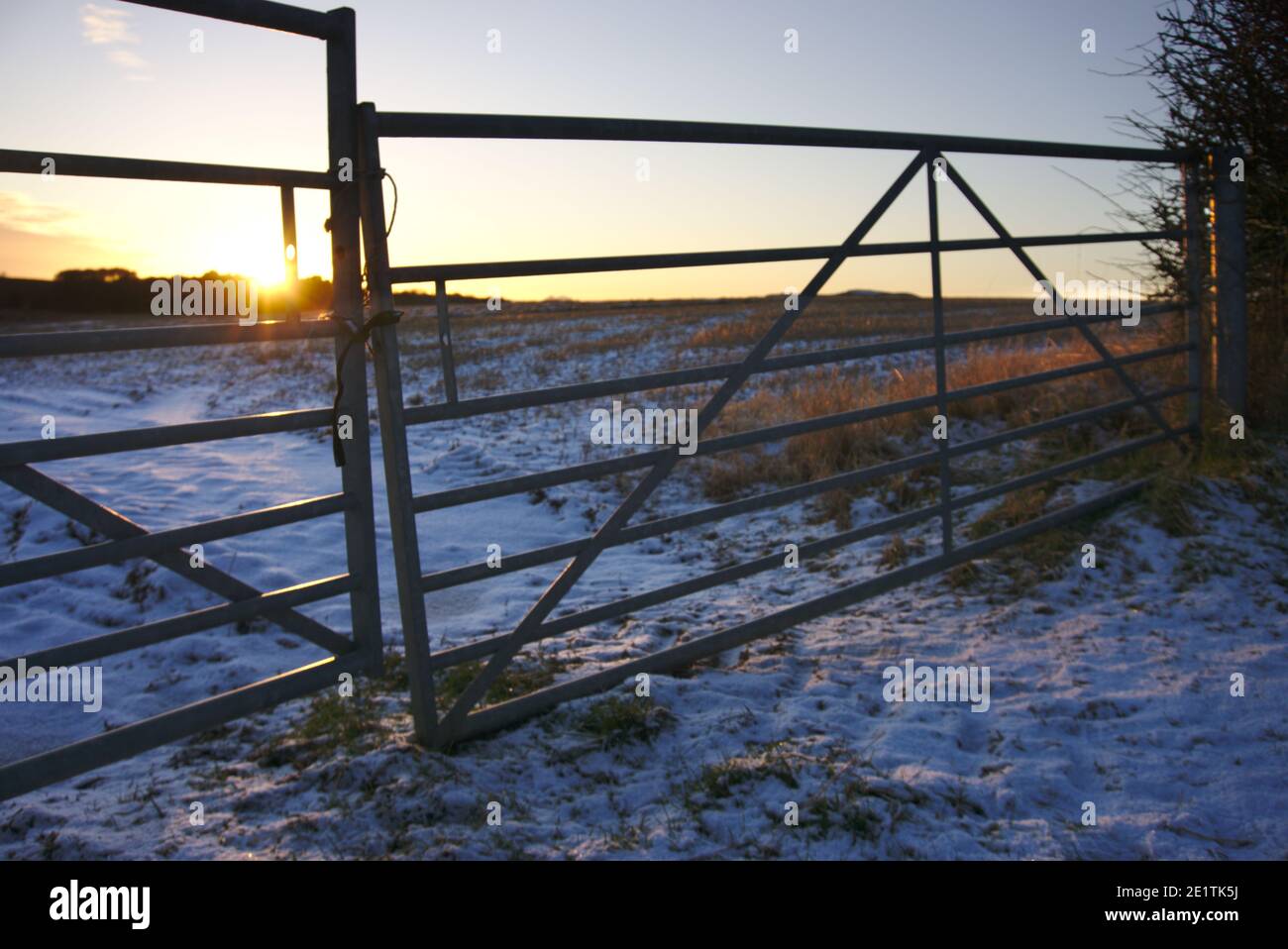Winter sunset seen through gate at the edge of a snow-covered field ...