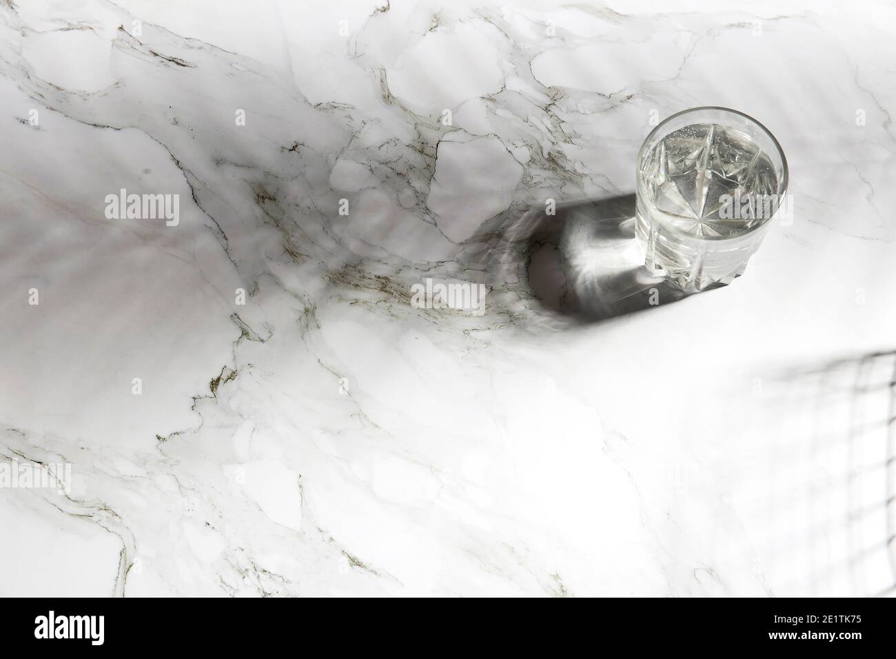A glass of cold water casting a shadow in hot weather on a marble table ...