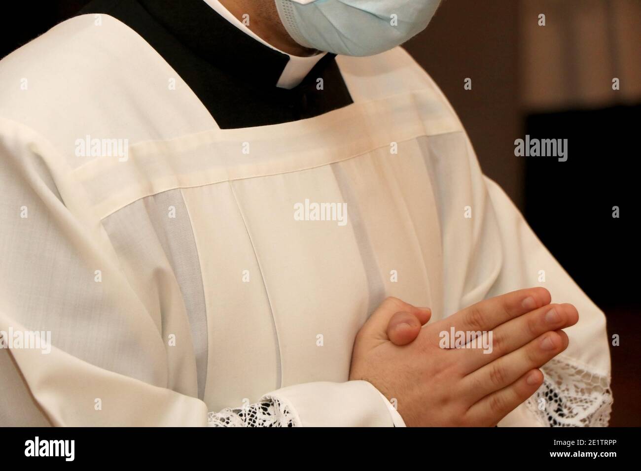 Young priest with hands folded in prayer wears surgical mask due to the ...