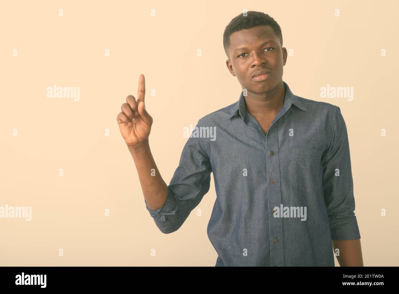 Studio shot of young black African man pointing finger up against white ...