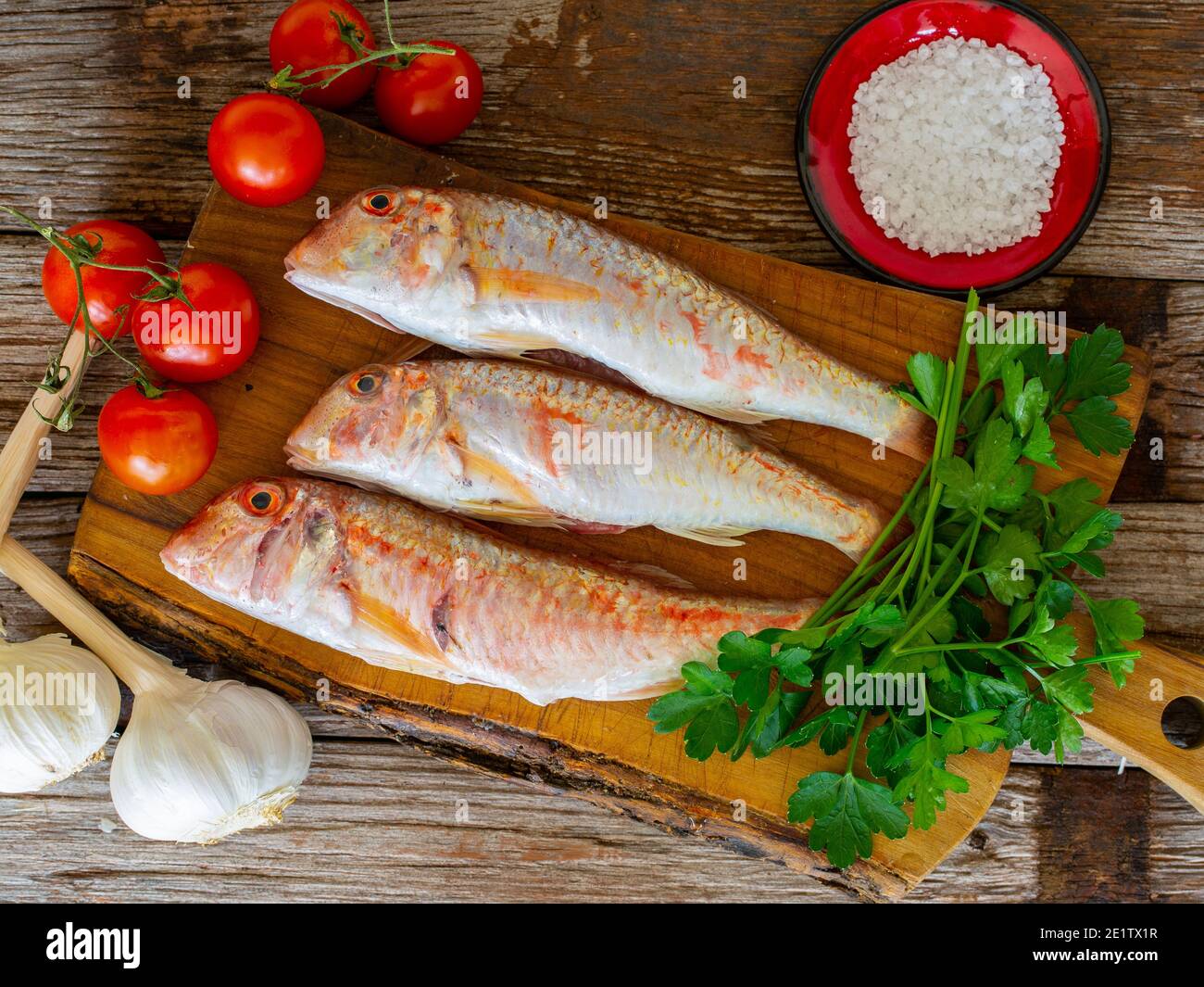 red mullet on an old wooden board background with typical ingredients ...