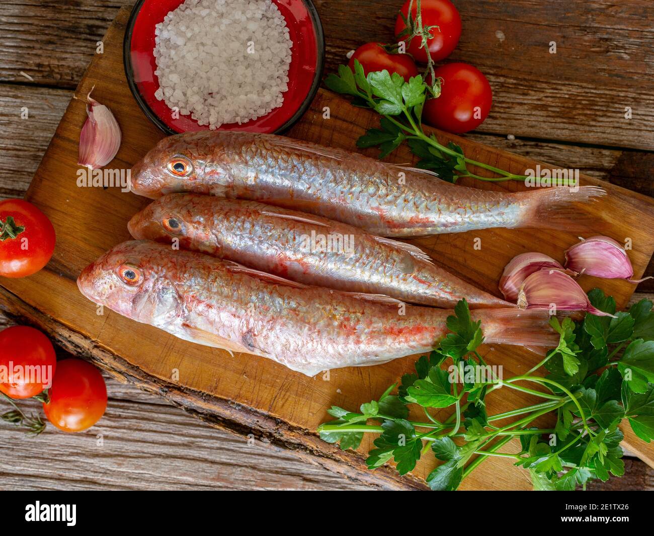 red mullet on an old wooden board background with typical ingredients ...