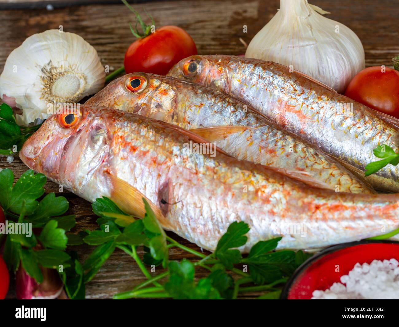 red mullet on an old wooden board background with typical ingredients ...