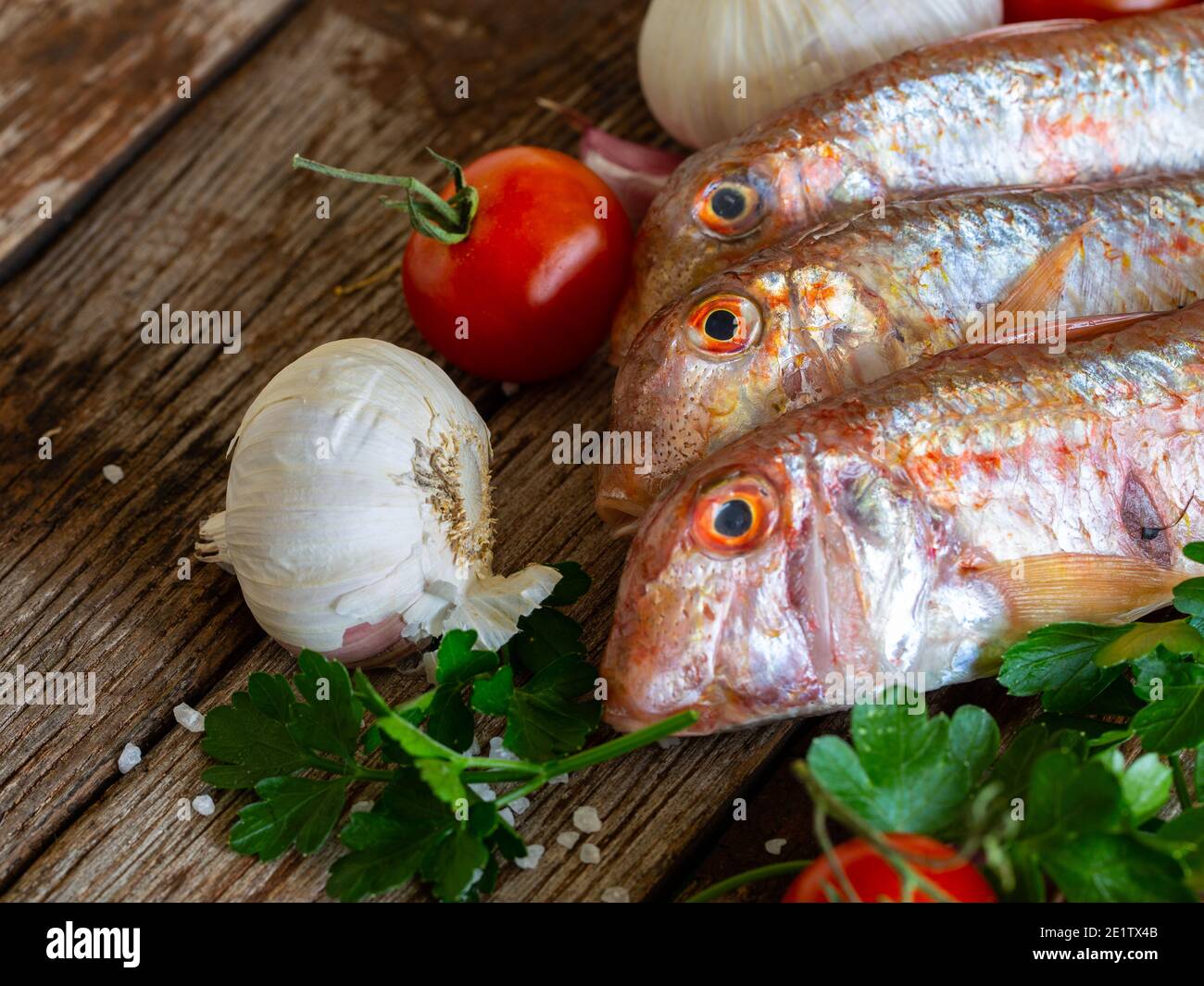 red mullet on an old wooden board background with typical ingredients ...