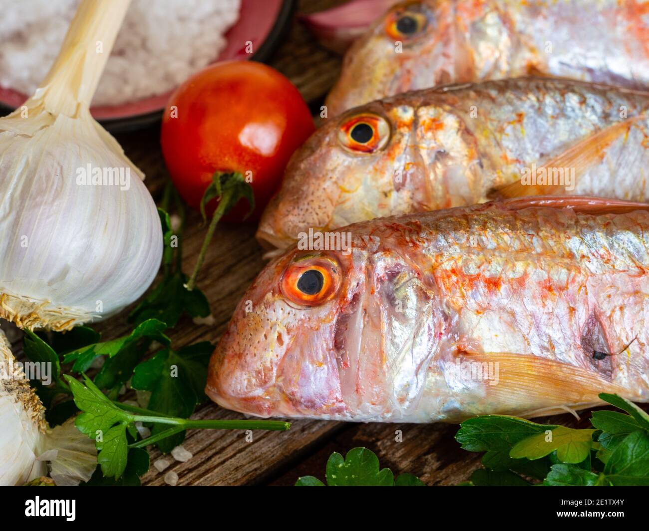 red mullet on an old wooden board background with typical ingredients ...