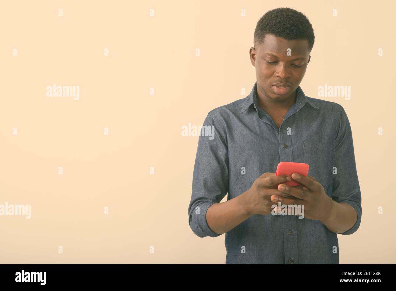 Studio shot of young black African man using mobile phone against white ...