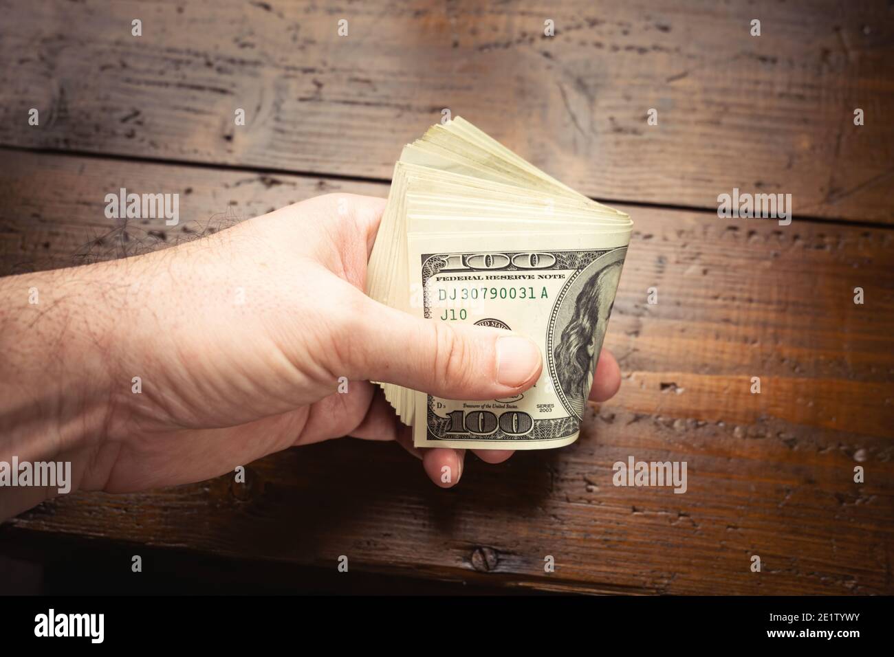 Hand holding one hundred US banknotes over wooden table background ...