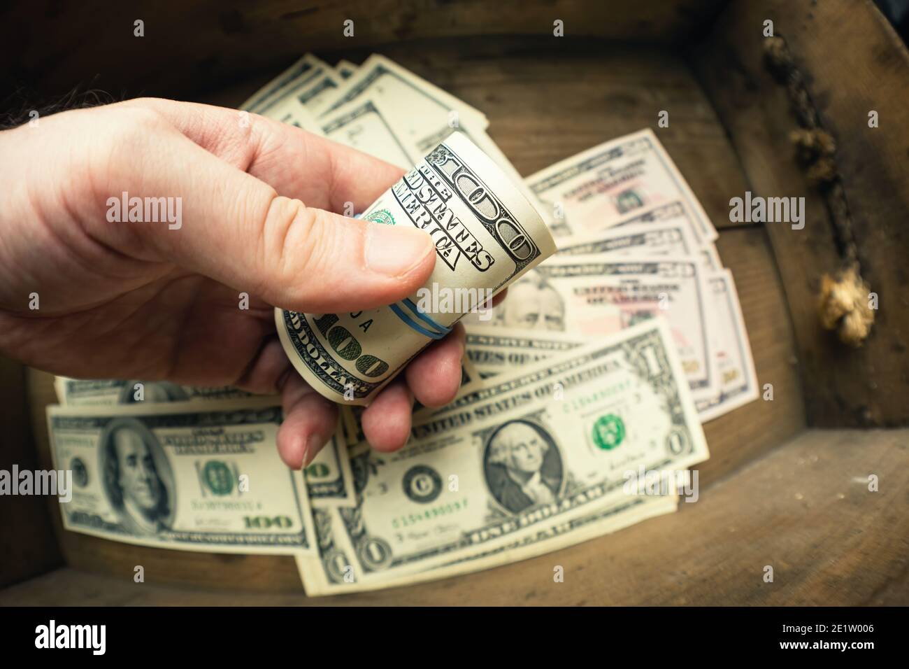 Hand holding one hundred US banknotes in roll over wooden drawer ...