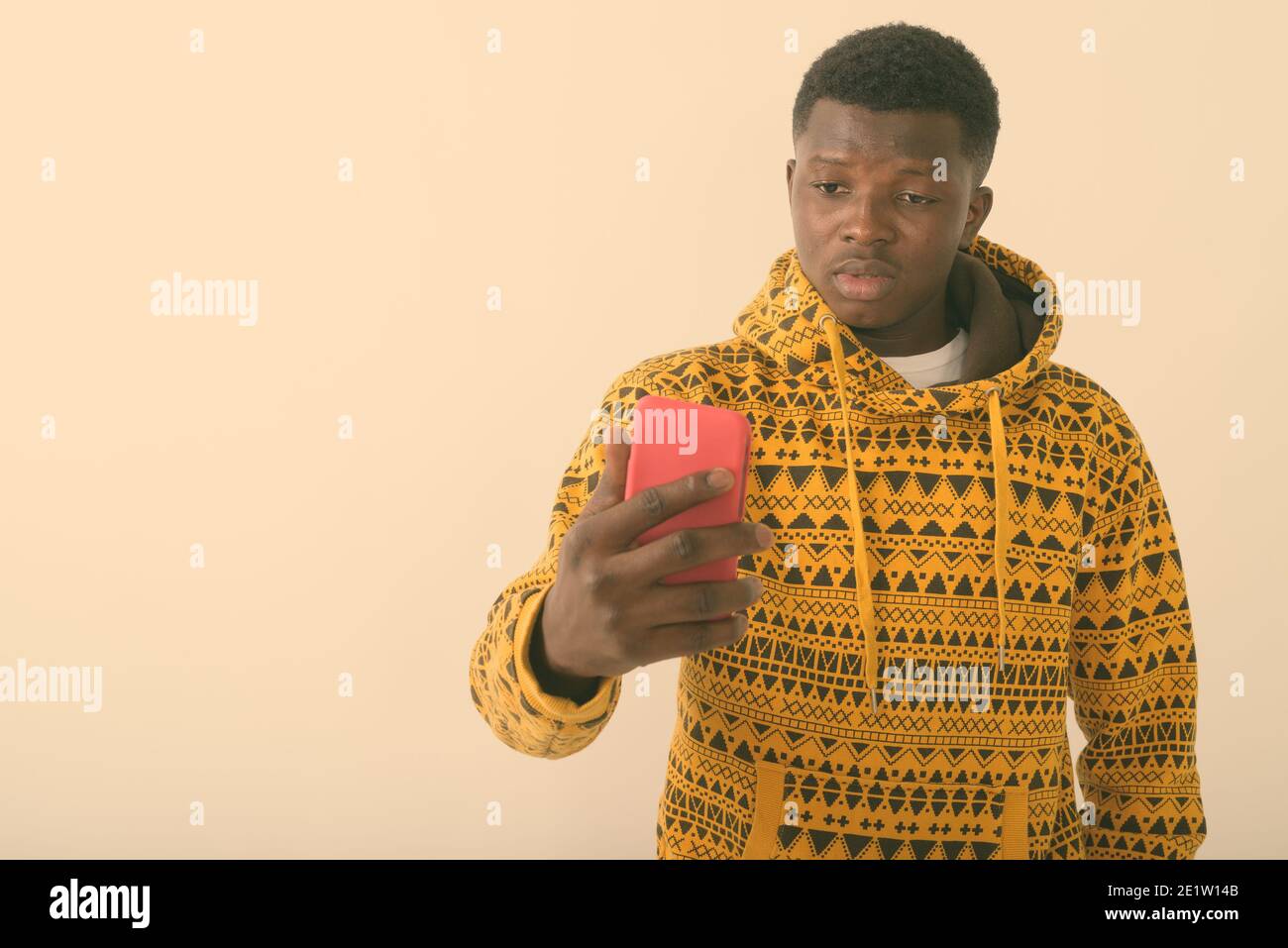 Studio shot of young black African man using mobile phone against white ...