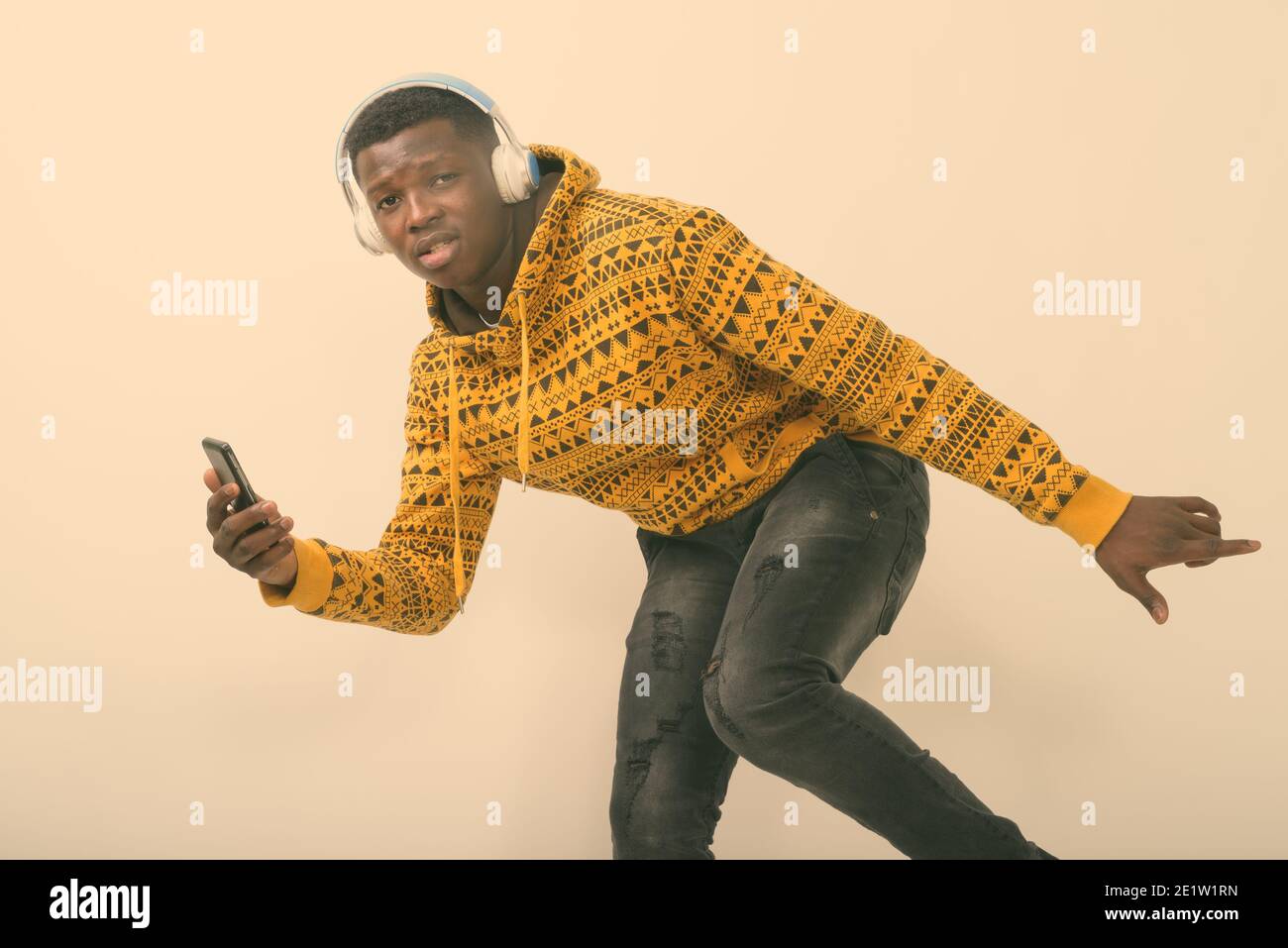 Studio shot of young black African man holding mobile phone while ...