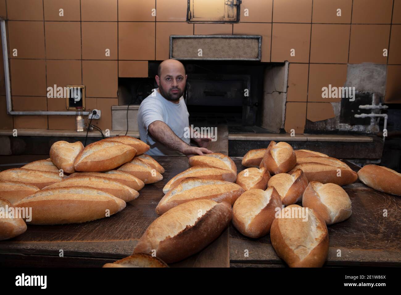 Baker. A young handsome bakery worker on the background of bread, takes ...
