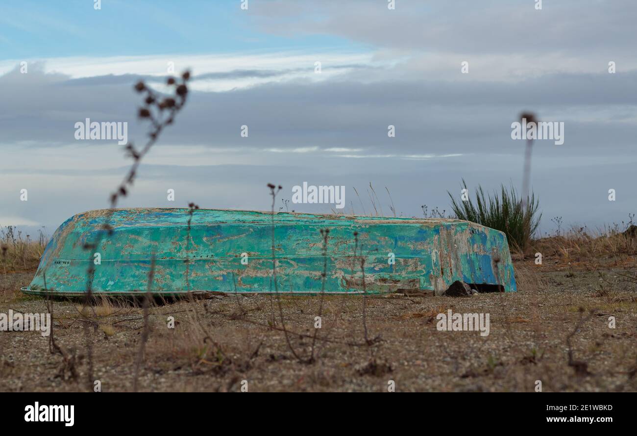 The old inverted green color boat lies on the sea shore in cloudy day ...