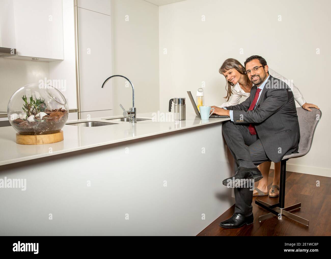 couple in a kitchen with man woking in his laptop and woman watching ...