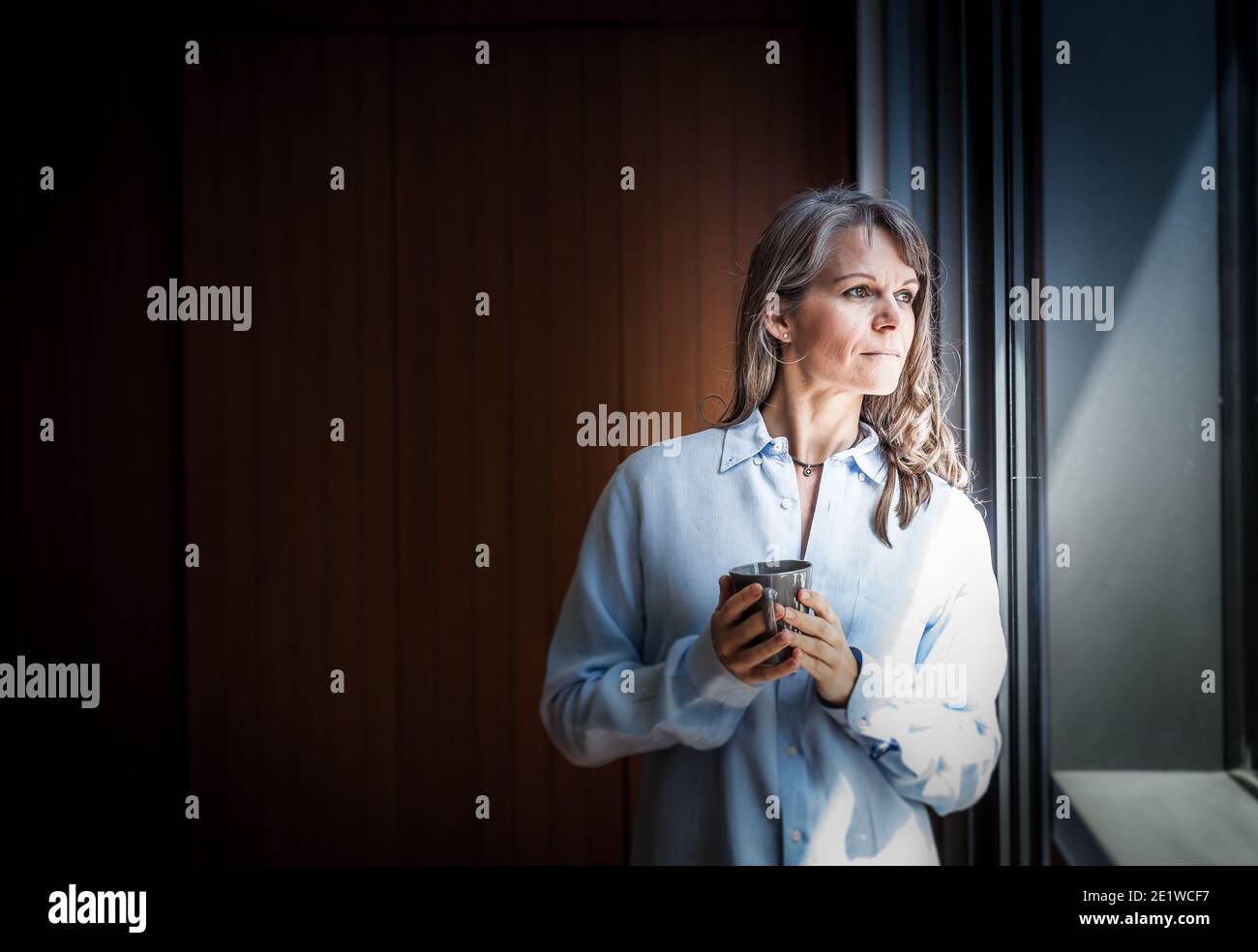 Gorgeous middle aged woman looking over the window and drinking her ...