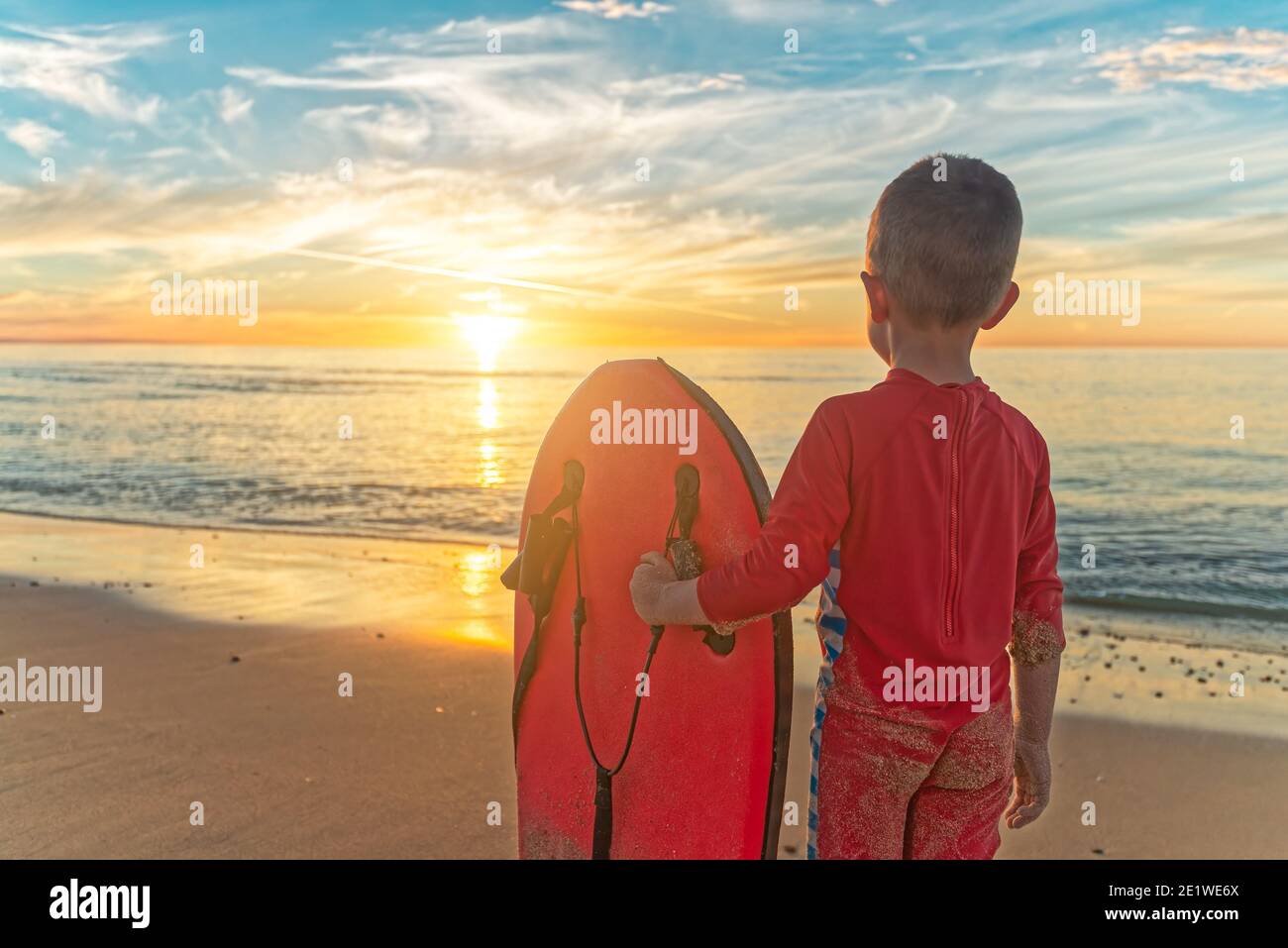 Cute boy holding bodyboard whilst standing at the beach and watching ...