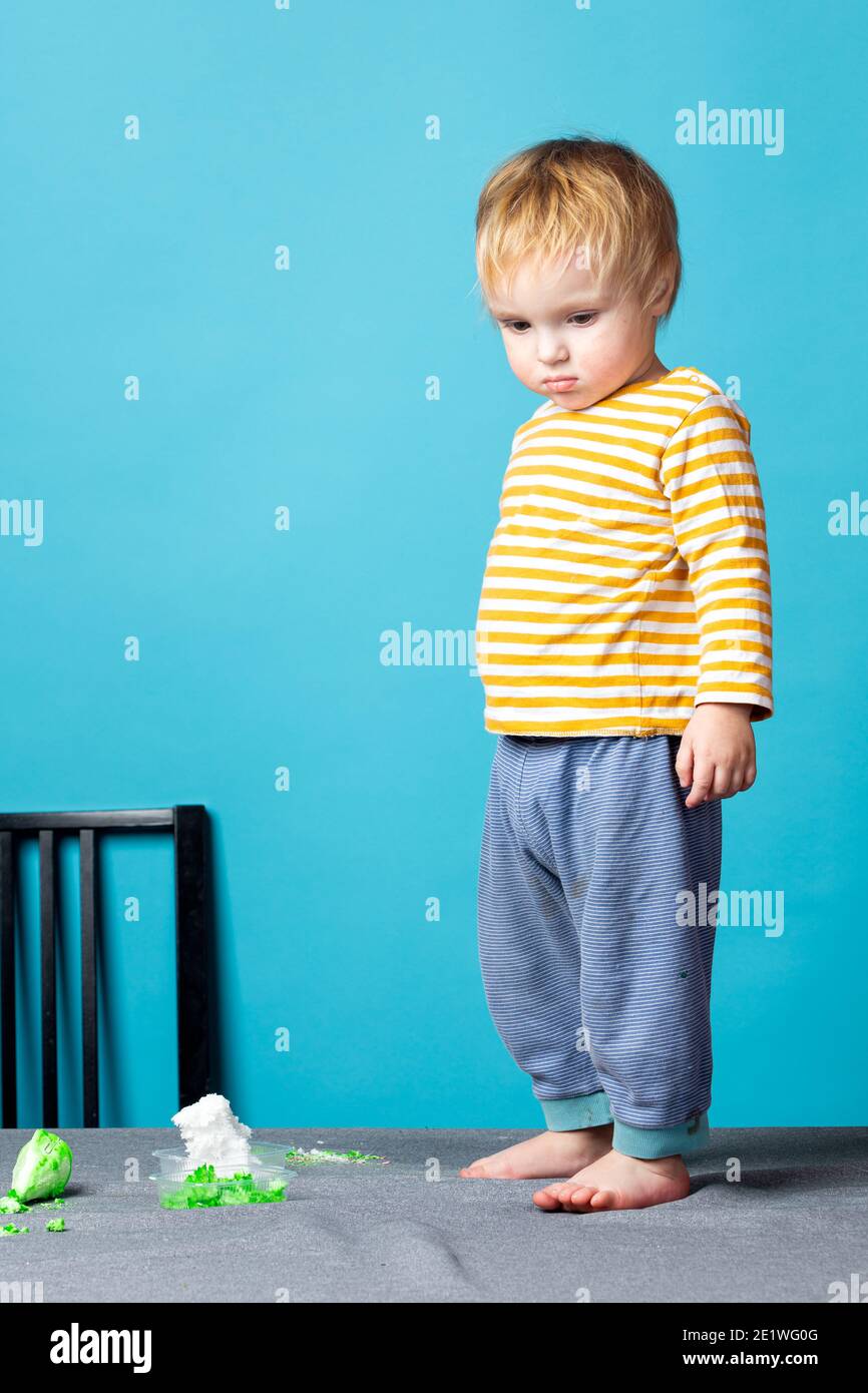 A little boy stands on the table and looks upset because he broke the ...