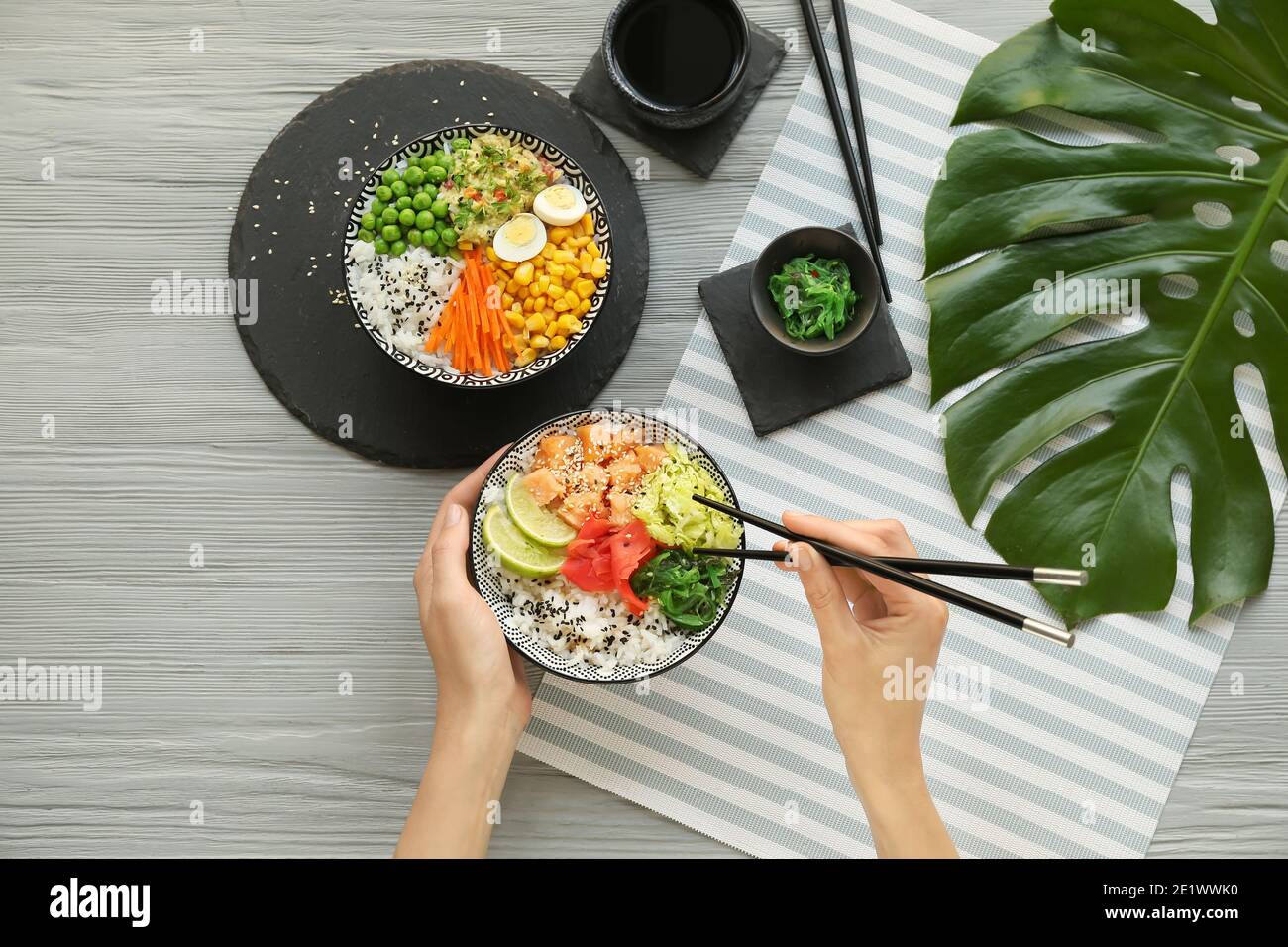Woman eating tasty rice poke bowl on wooden background Stock Photo - Alamy
