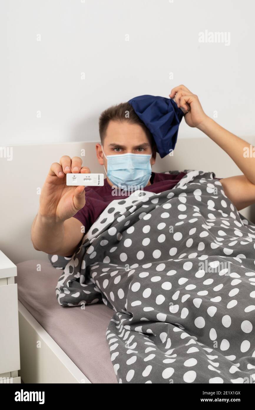 Covid-19 male patient lying in bed at home is holding a rapid antigen ...
