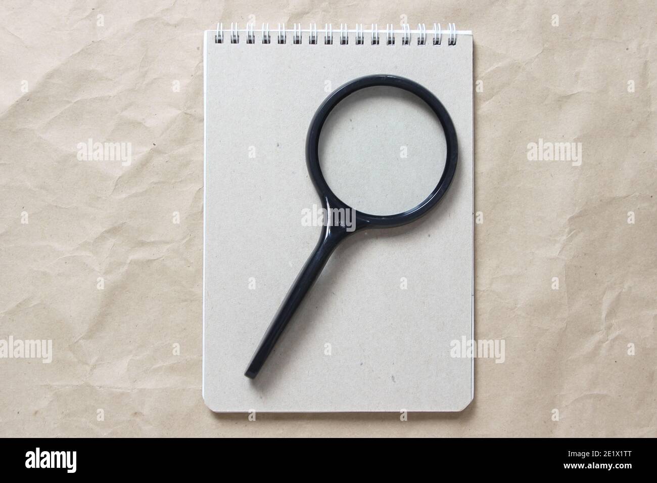 Gray notepad with white coiled spring and magnifier on a background of ...