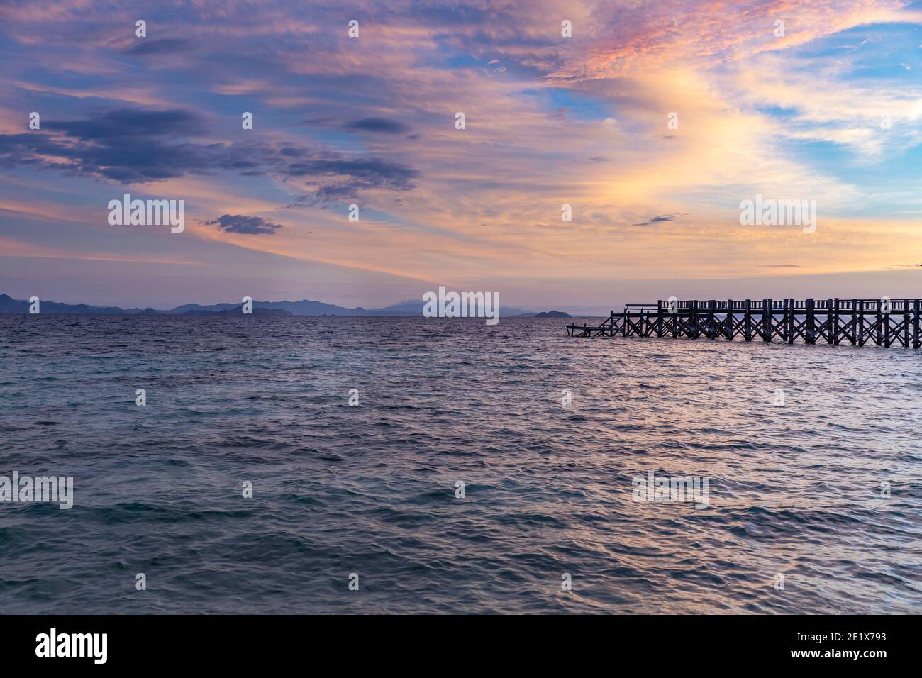 silhouette of a wooden jetty at sunset with blue soft waves in the fore ...