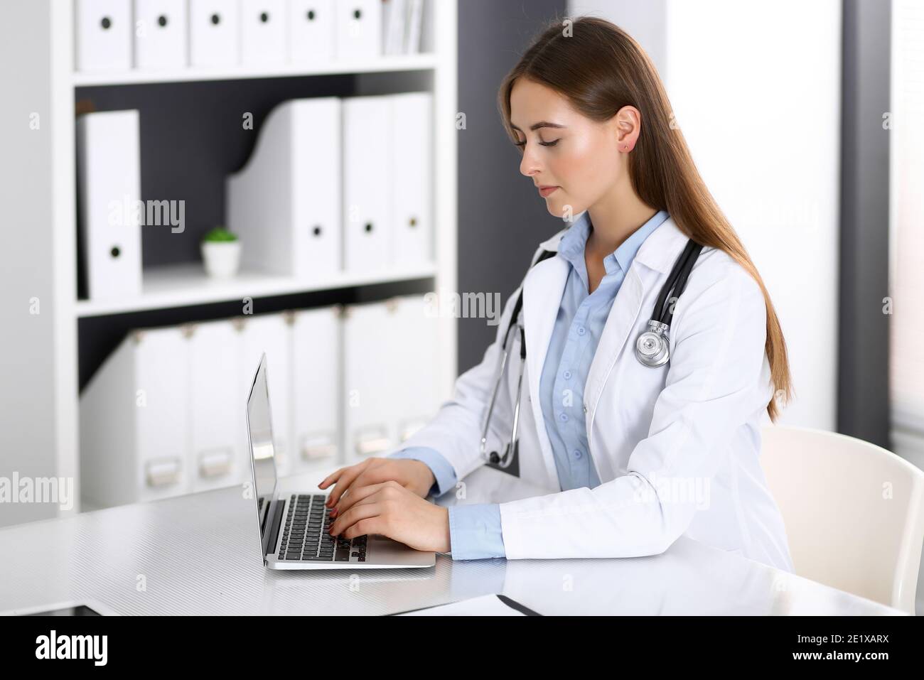 Doctor woman typing on laptop computer while sitting at the desk in ...
