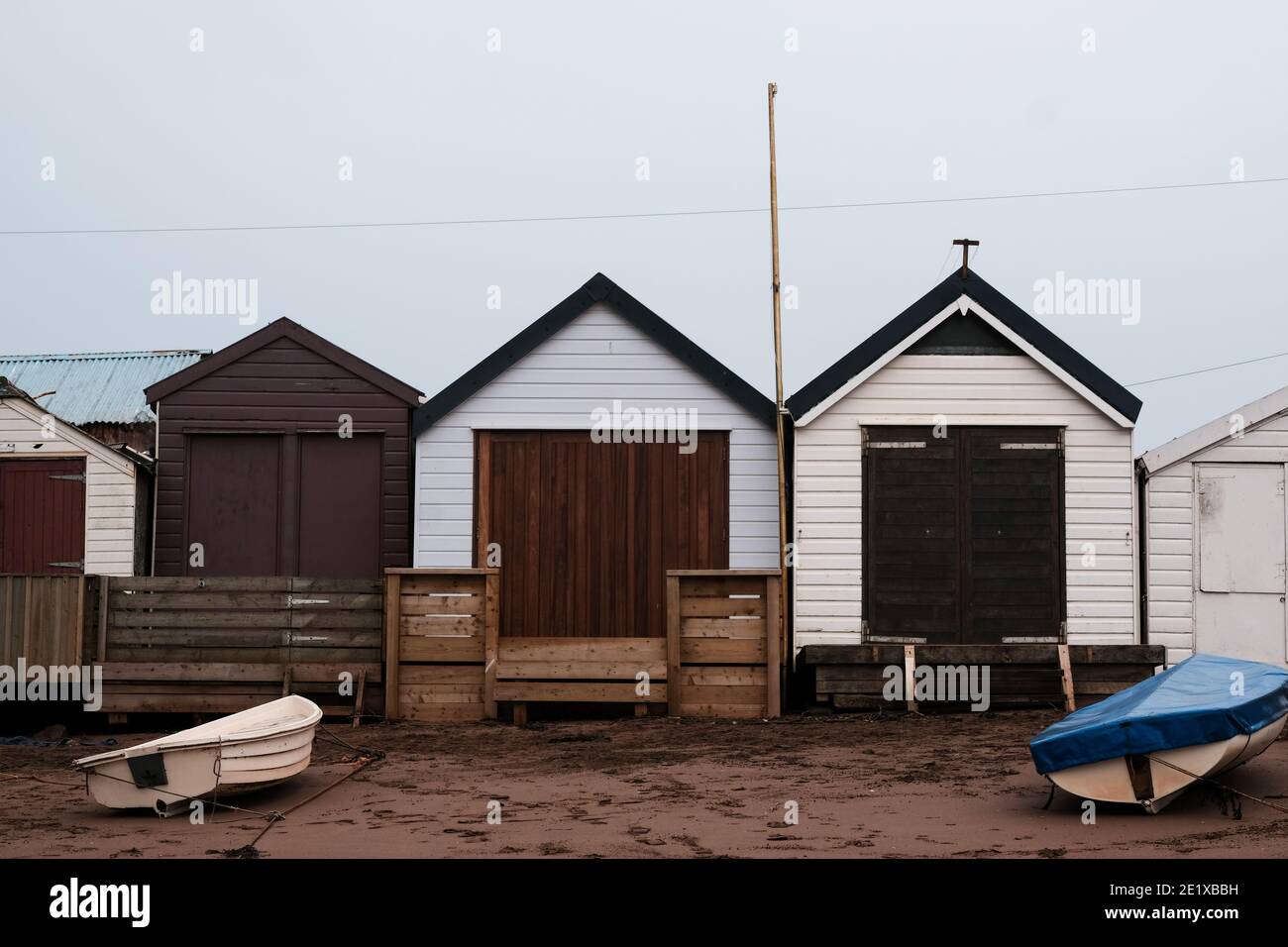Beach huts and little wooden boats on the sand in Teignmouth during an ...