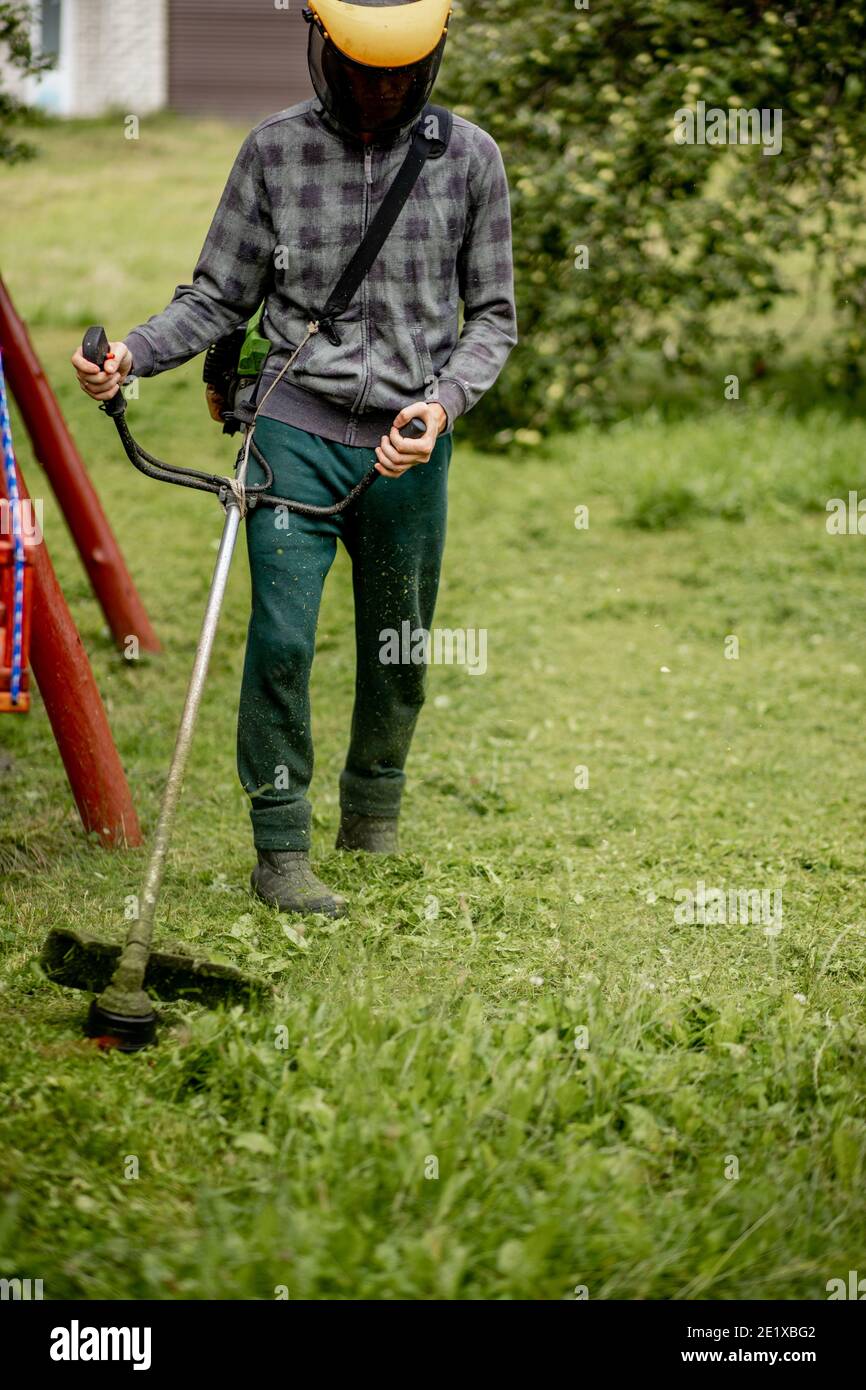 Worker with a gas mower in his hands, mowing grass in front of the ...