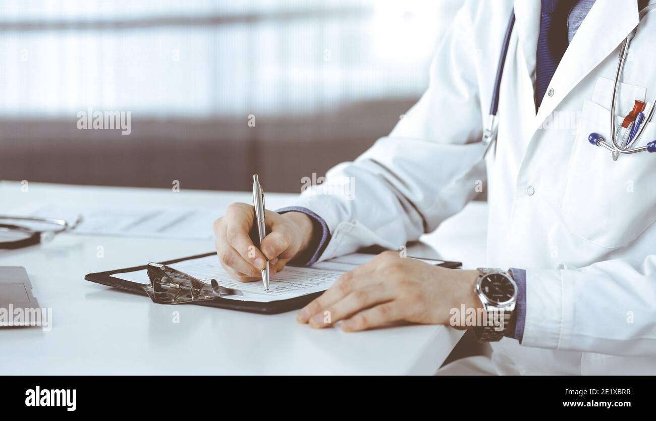 Unknown male doctor sitting and working with clipboard of medication ...