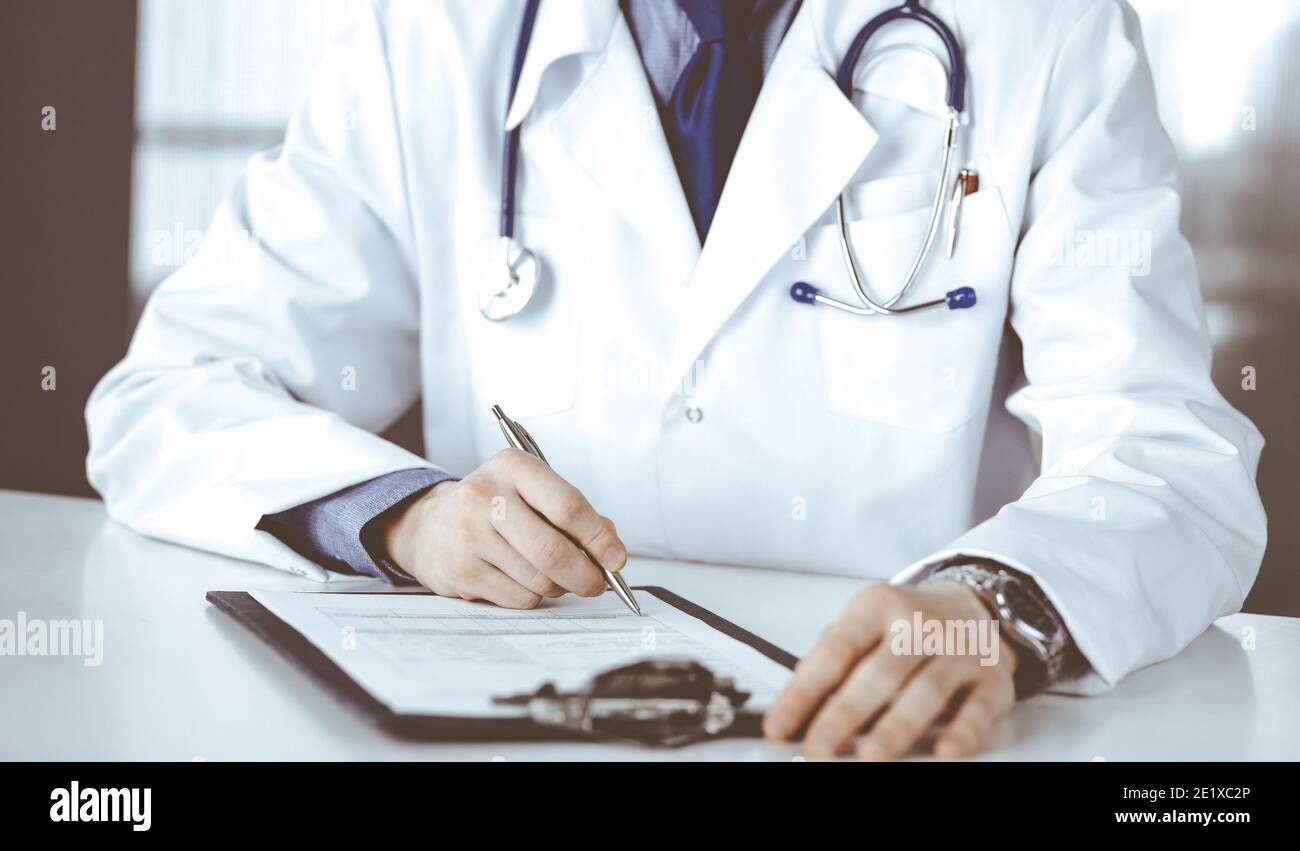 Unknown male doctor sitting and working with clipboard in clinic at his ...