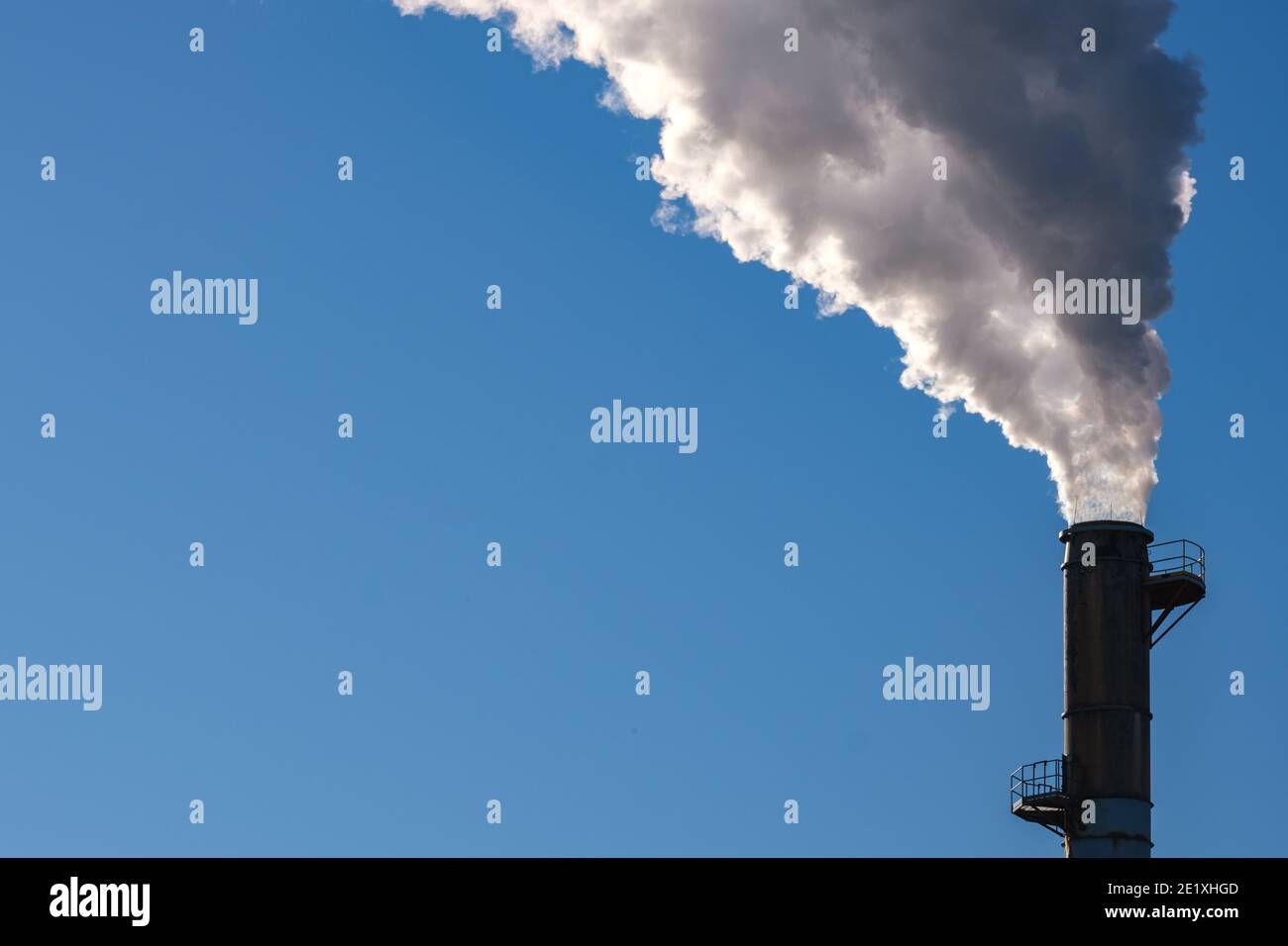 Thick smoke billows into a clear blue sky from the top of a tall ...